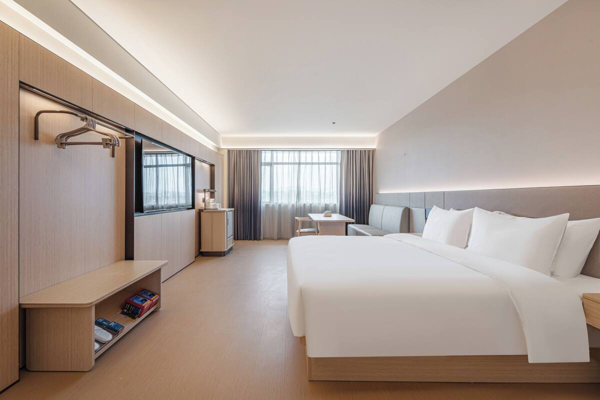 Quarto de hotel moderno com uma cama grande, mesa de cabeceira, escrivaninha e guarda-roupa.