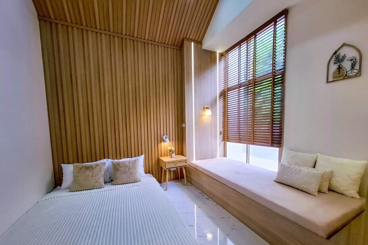 Quarto com cama, mesa de cabeceira, banquinho e janela com persianas.
