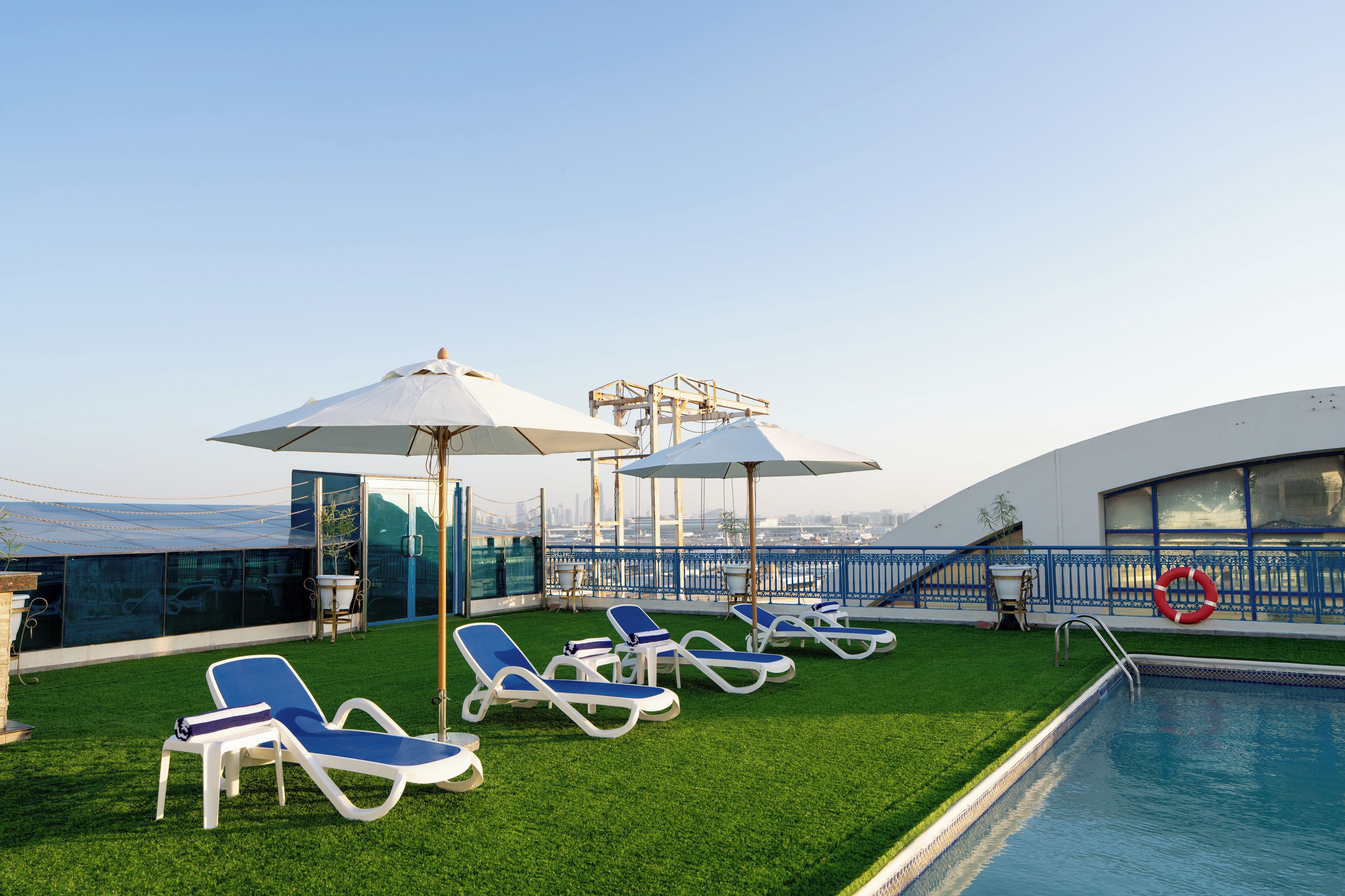 Uma área de piscina no terraço com espreguiçadeiras e guarda-sóis, um espaço envidraçado e vista para o horizonte da cidade.