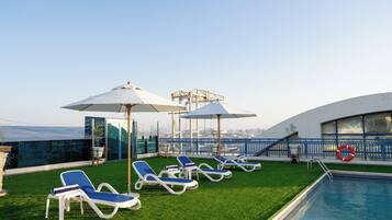 Uma área de piscina no terraço com espreguiçadeiras e guarda-sóis, um espaço envidraçado e vista para o horizonte da cidade.