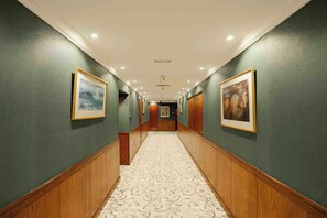 Corredor com paredes verdes, lambris de madeira e carpete estampado.