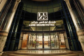 A entrada do LUXE GRAND HOTEL, com fachada de vidro e uma placa chamativa.