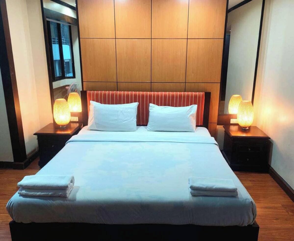 Uma cama de casal bem arrumada com lençóis brancos, duas luminárias de cabeceira e uma cabeceira de madeira.