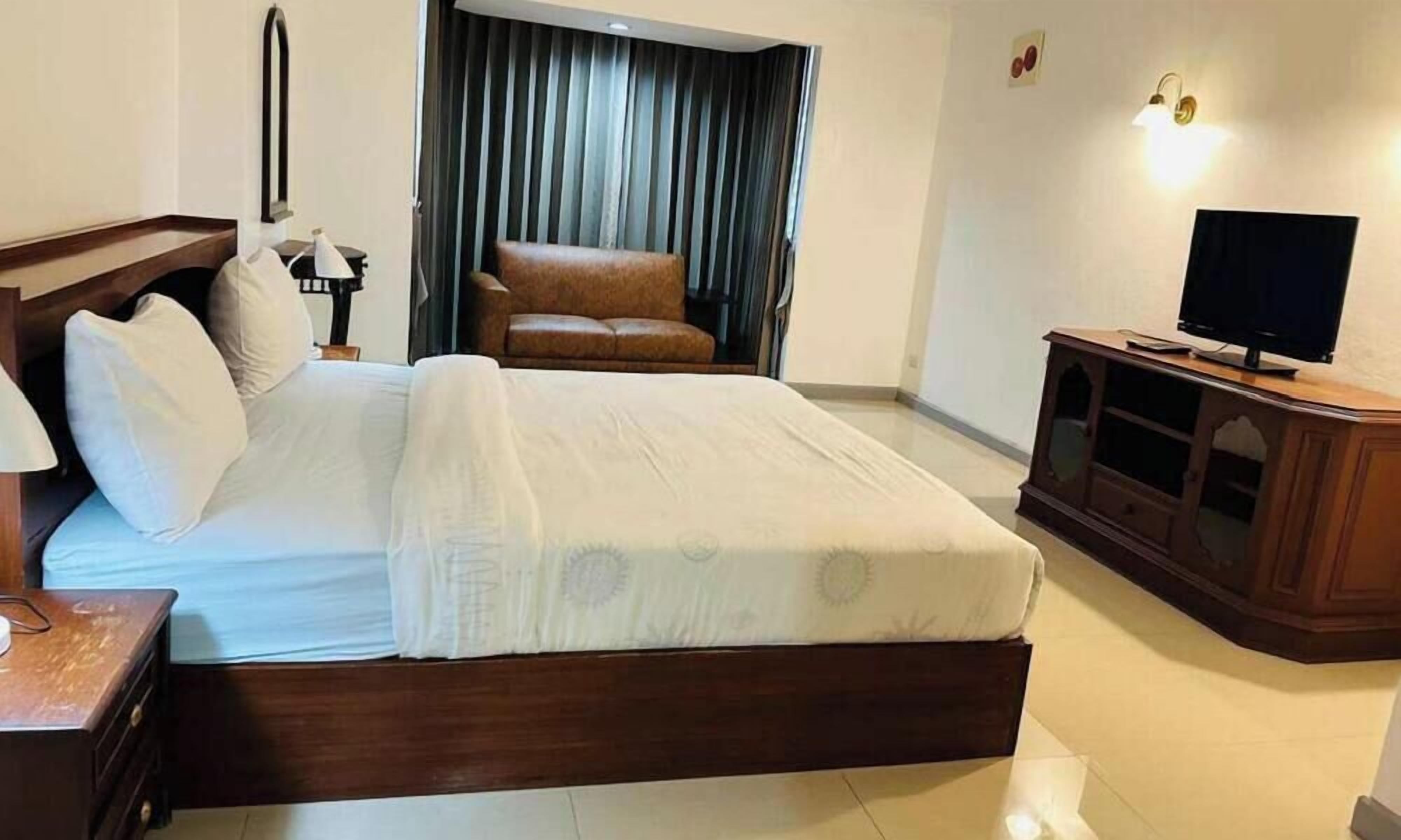 Quarto de hotel com uma cama grande, televisão, escrivaninha e sofá.
