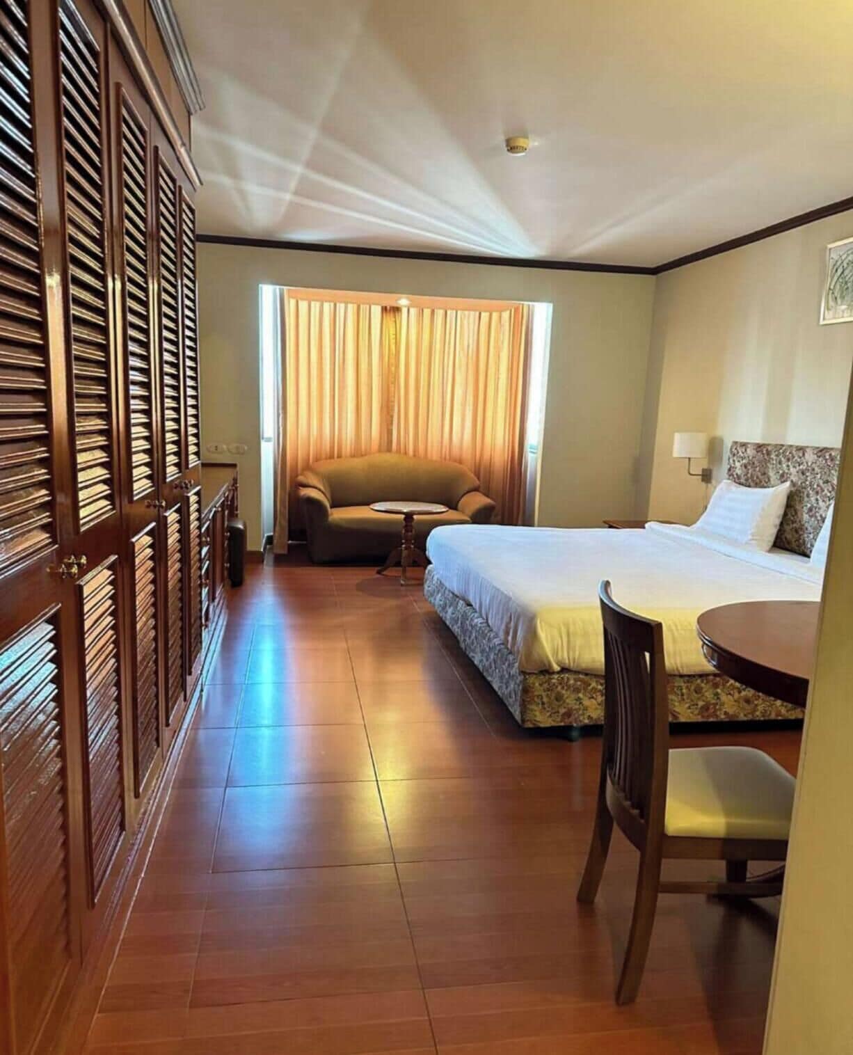 Quarto de hotel com cama, cadeira, mesinha, sofá e janela com cortinas.