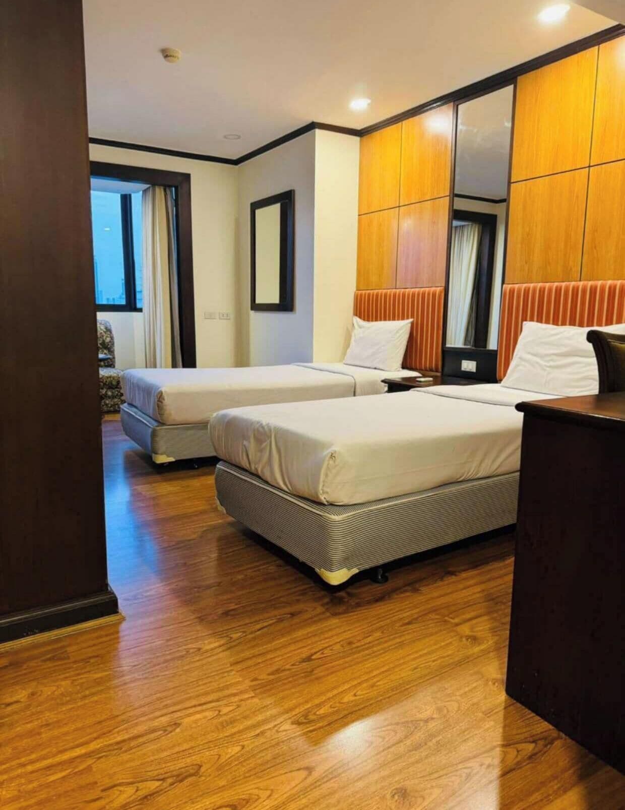 Quarto de hotel com duas camas, um espelho grande, piso de madeira e vista para a cidade.