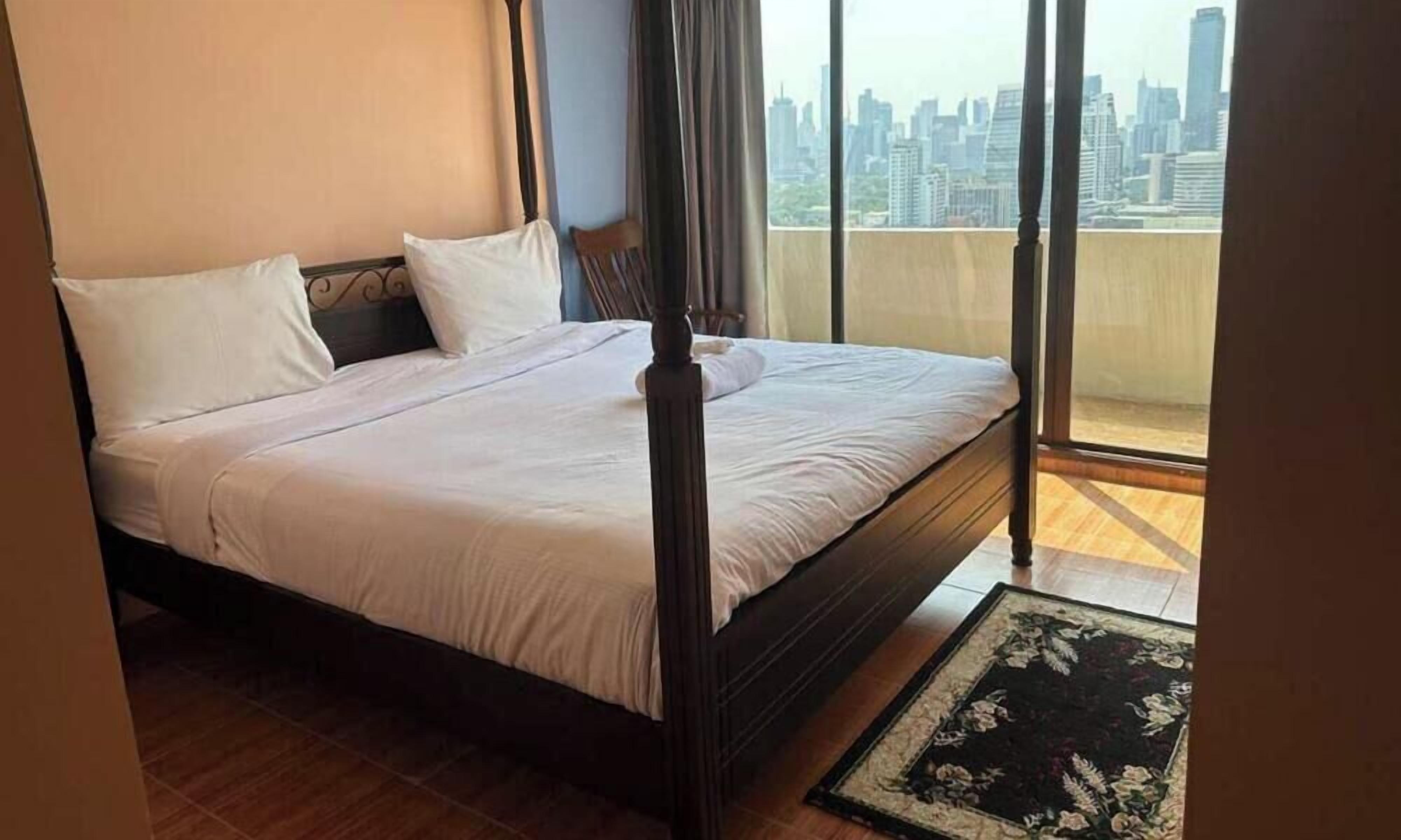 Cama com dossel e roupa de cama branca, piso de madeira e vista para o horizonte urbano através de uma grande janela.