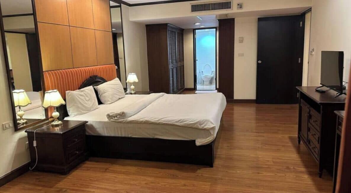 Quarto de hotel com cama, mesas de cabeceira, cômoda, televisão e porta para uma varanda.