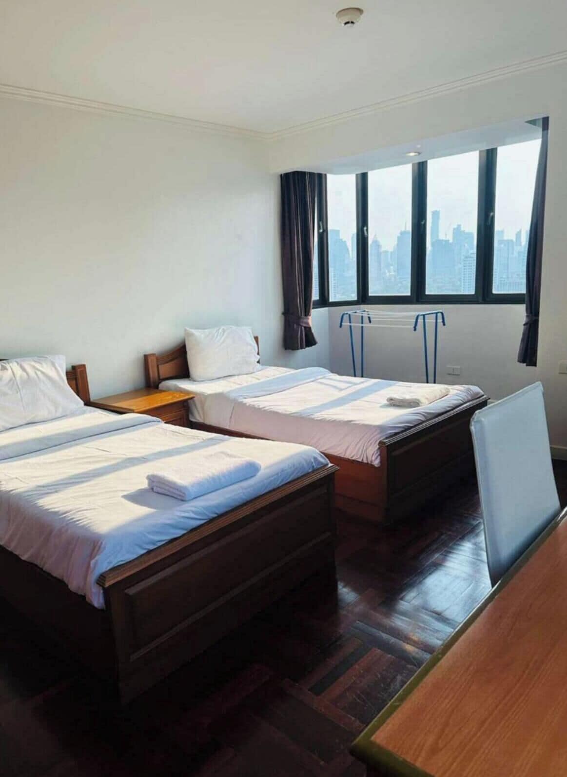 Quarto de hotel com duas camas, vista da cidade através de grandes janelas e piso de madeira.