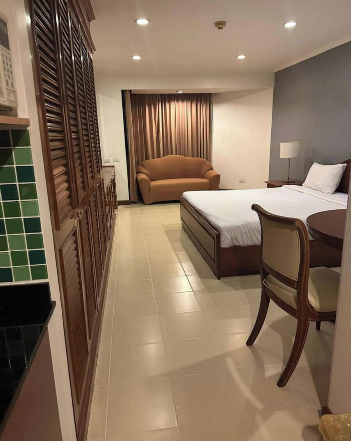 Quarto de hotel compacto com cama, sofá pequeno, mesa de jantar com cadeiras e janela com cortinas.