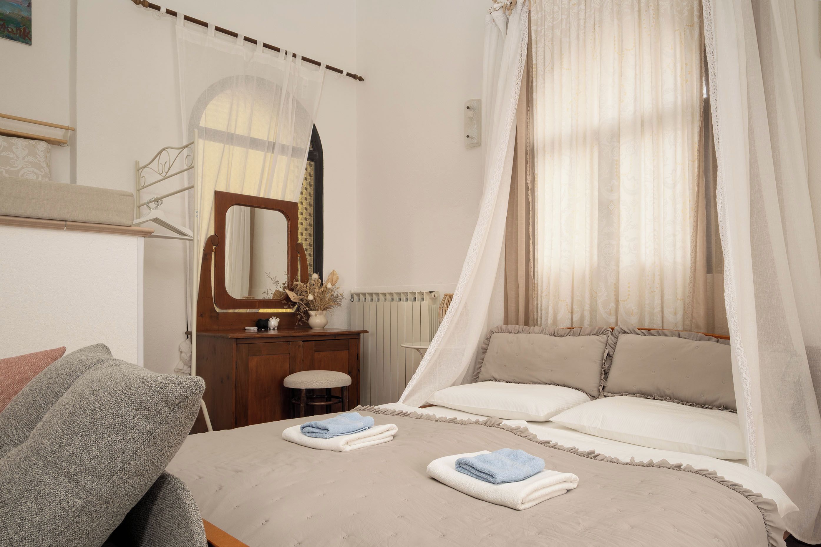 Quarto com cama, mesa de cabeceira, espelho e janela com cortinas.