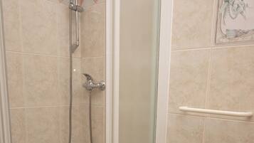 Chuveiro com porta de vidro, banheira branca e vaso sanitário.