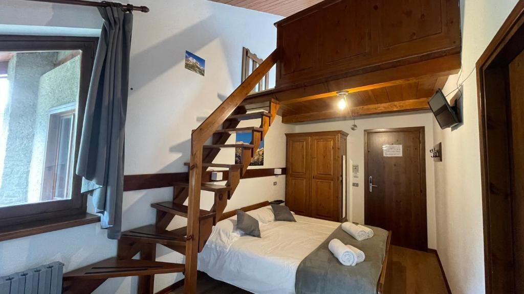 Um quarto com uma cama, escada de madeira, porta e janela.