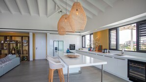 Cozinha moderna com ilha central, luminárias pendentes e vista para a cidade através de amplas janelas.