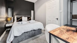Quarto moderno com cama, mesa de cabeceira, abajur e uma pequena mesa de madeira.