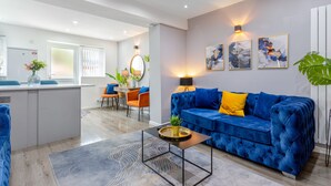 Uma sala de estar moderna com um sofá azul, uma mesa de centro e um espaço de refeições com uma cadeira e uma mesa.