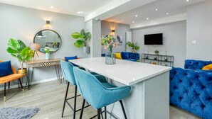 Uma cozinha moderna com uma ilha central, banquetas e um espaço de estar com um sofá azul.
