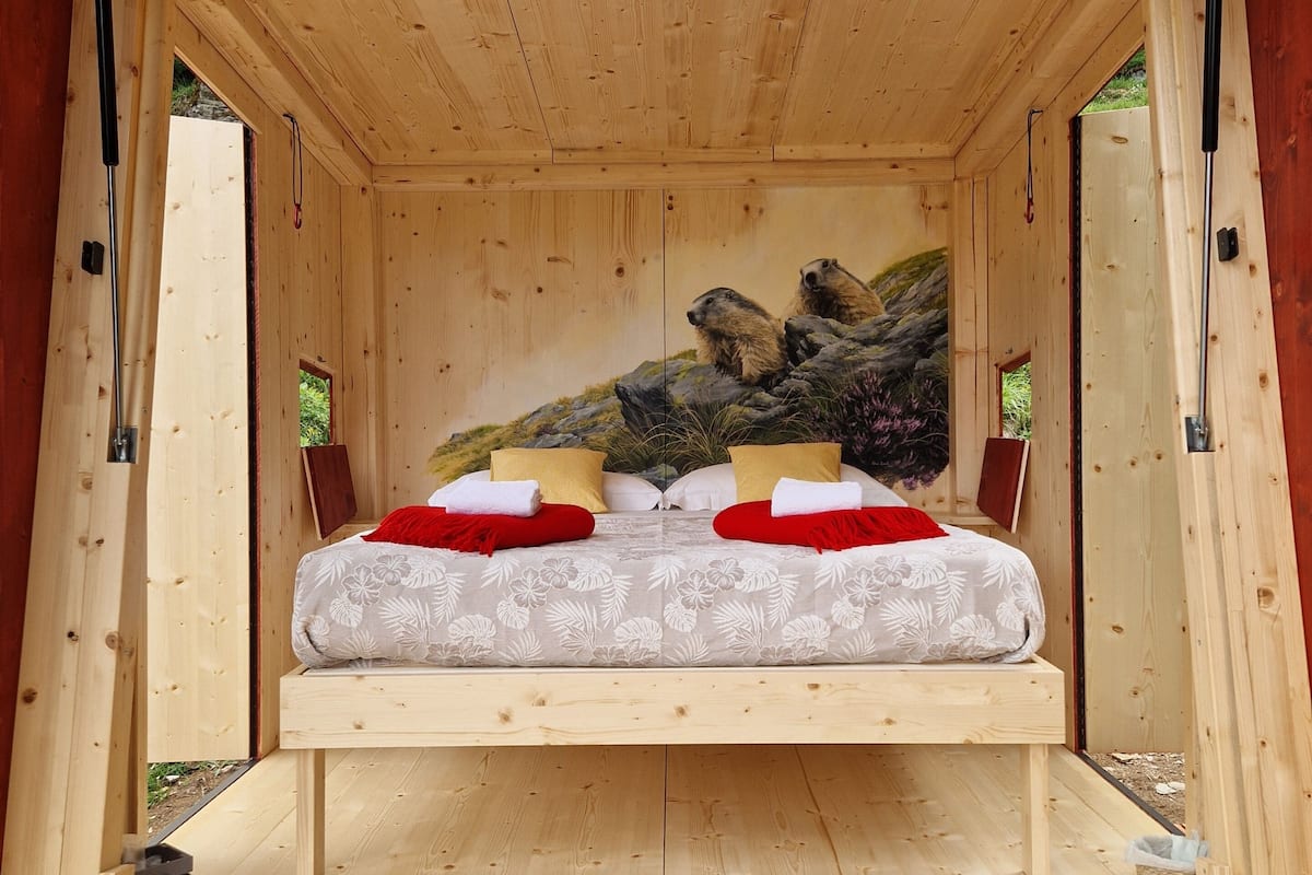 Uma cabana de madeira com uma cama, um quadro de uma montanha e vista para o exterior.
