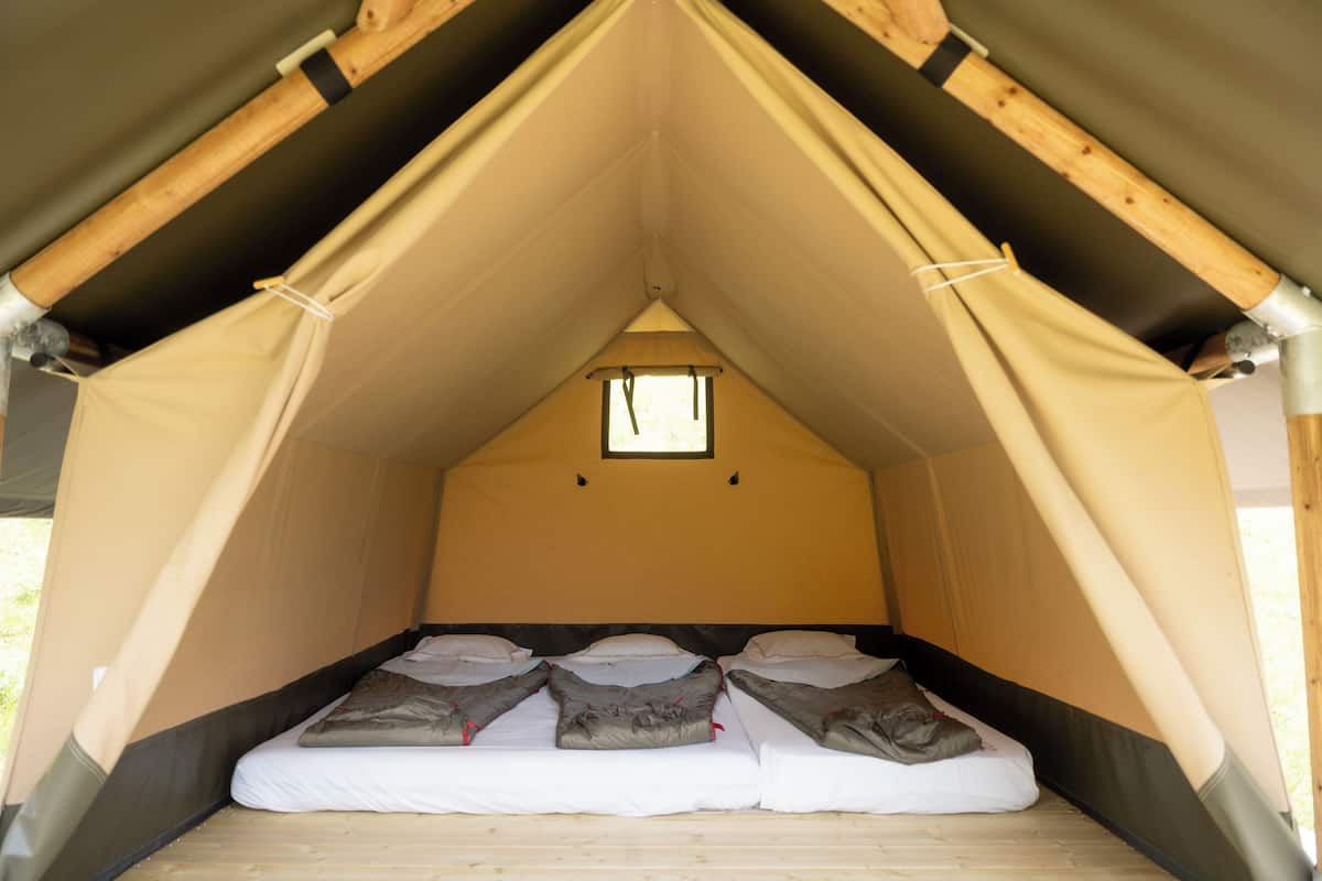 Uma tenda com telhado inclinado, uma janela e uma cama com almofadas e cobertor.