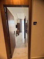 Um corredor de hotel com porta de madeira, placa de número e vista para um quarto com cama e janela.