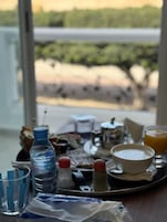 Uma bandeja com itens de café da manhã, incluindo uma tigela de cereal, um copo de suco de laranja, uma garrafa de água e condimentos.