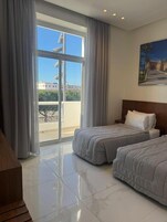Quarto de hotel com duas camas, uma janela grande com cortinas, um quadro na parede e vista para o exterior.