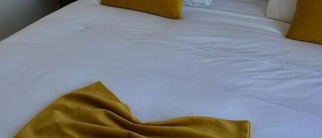 Quarto de hotel com cabeceira de madeira, roupa de cama branca e um cobertor amarelo mostarda.