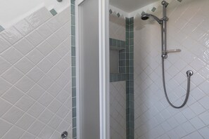 Casa de banho com paredes em azulejos brancos e verdes, chuveiro com duche manual e puxador de porta visível.
