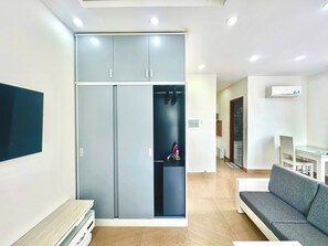 Uma sala de estar moderna com um sofá cinzento, uma televisão de ecrã plano na parede e um guarda-roupa embutido com espelho.