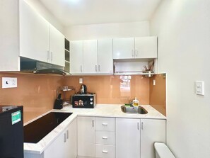 Uma cozinha compacta com armários brancos, micro-ondas preto, pia e fogão.