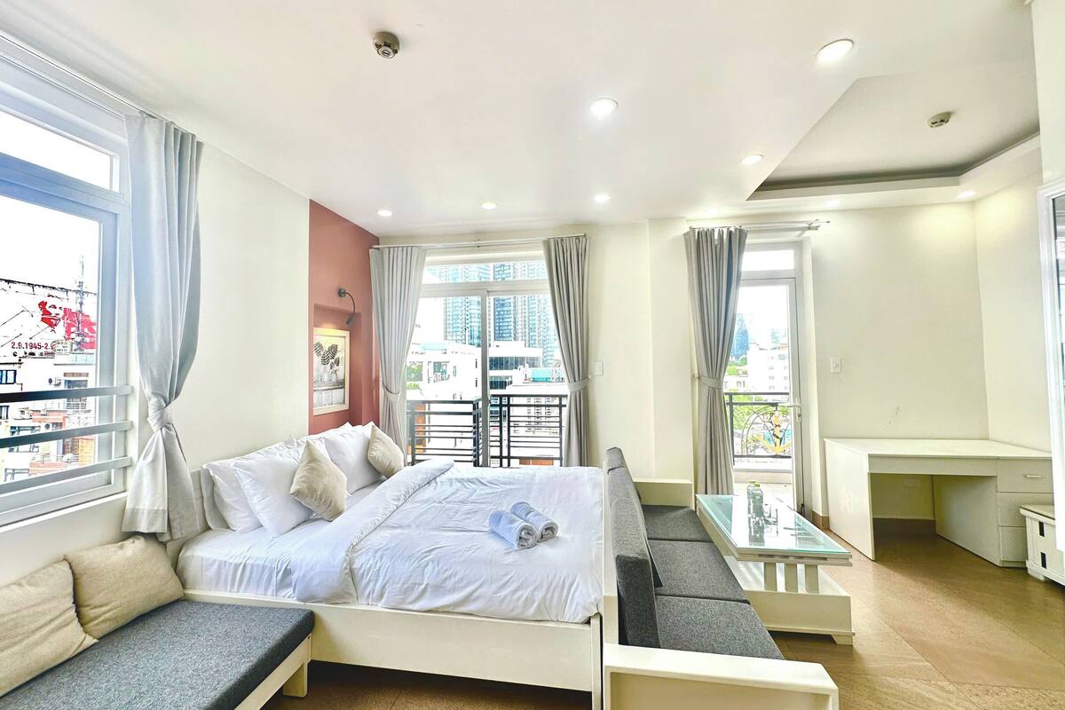 Quarto de hotel moderno com cama, área de estar e varanda com vista para a cidade.