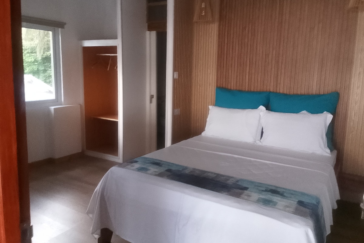 Um quarto com cama, janela, armário e parede de madeira.