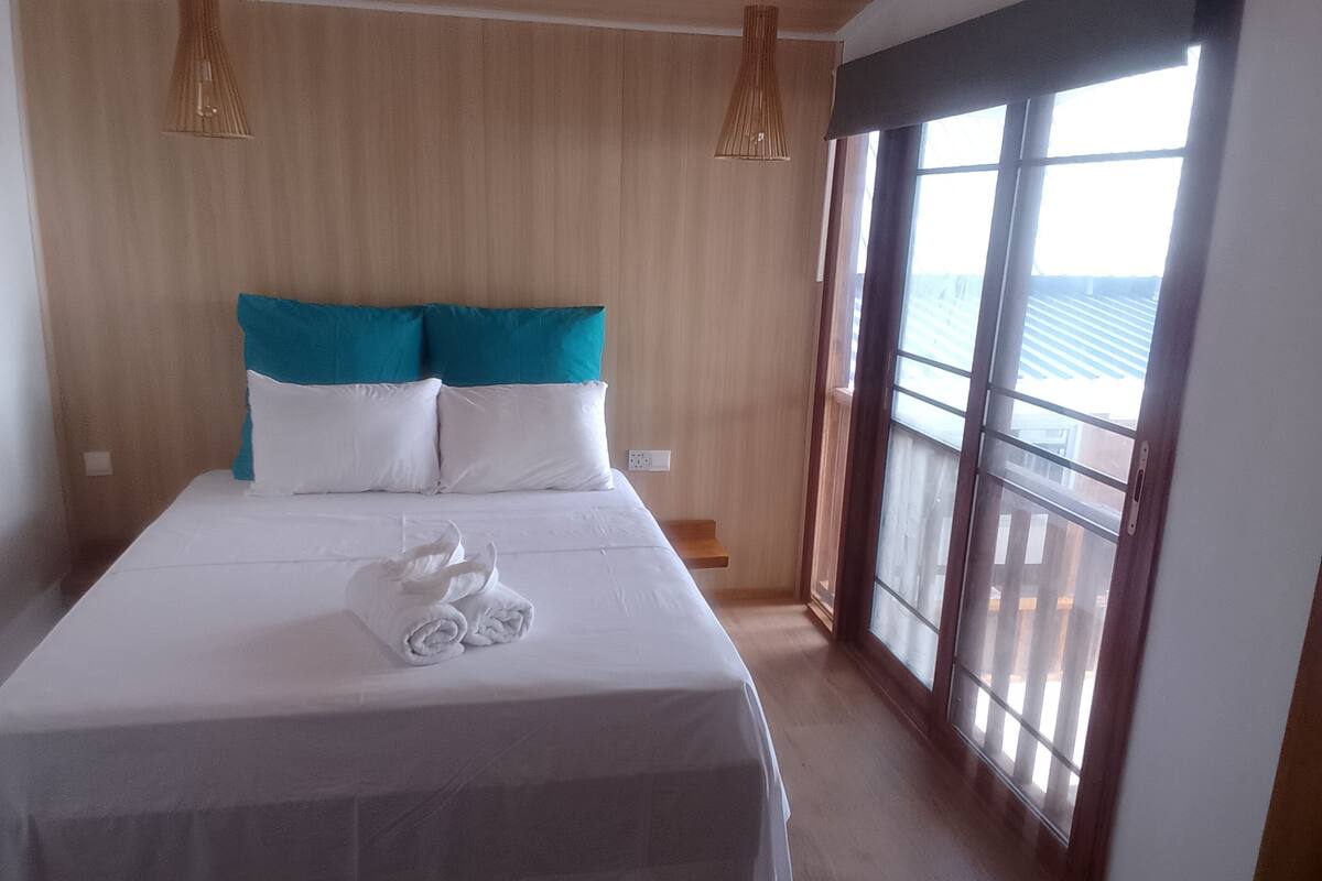 Quarto de hotel com cama, vista para o mar através de grandes janelas e varanda.