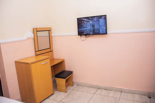 Quarto pequeno com um armário de madeira, um banquinho, televisão na parede e chão ladrilhado.