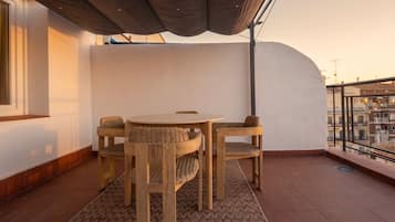 Terraço com mesa redonda e quatro cadeiras, tapete tecido e vista para a cidade.
