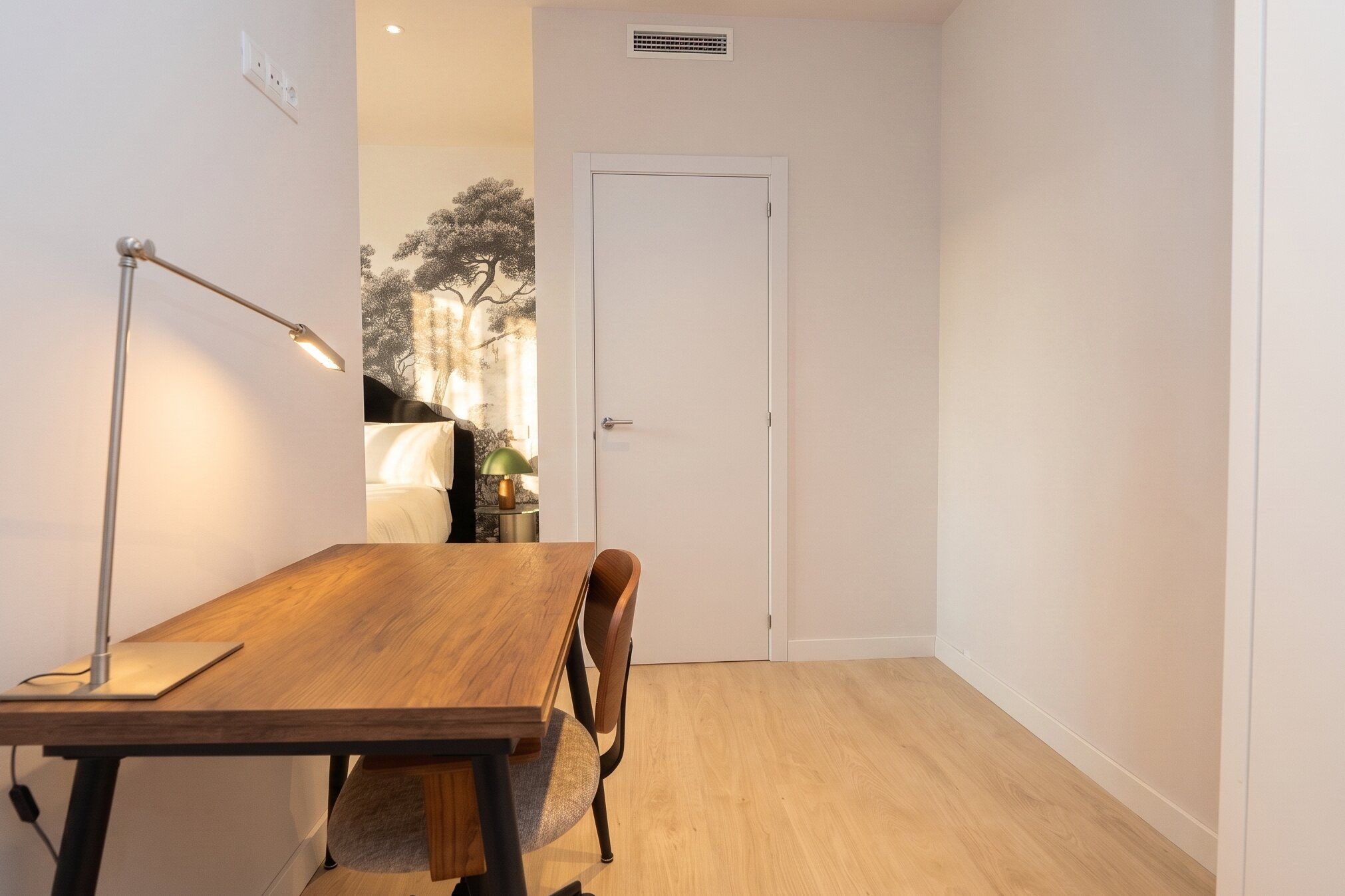 Uma área de refeições com uma mesa de madeira, cadeiras, uma luminária de mesa e um aplique na parede.