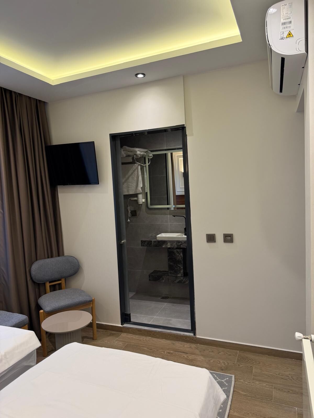 Quarto de hotel com cama, cadeira, televisão, chuveiro e ar condicionado.