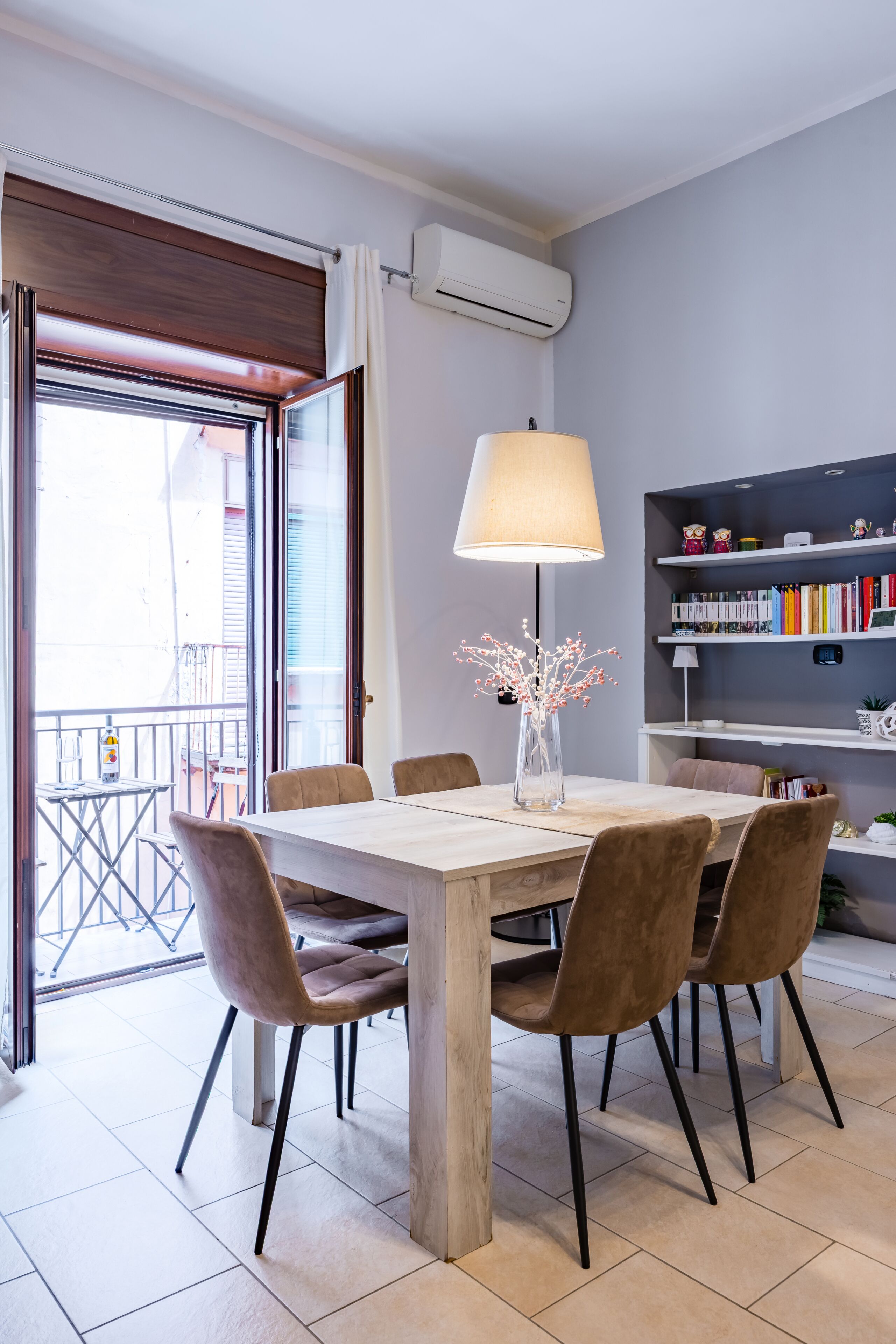 Uma área de refeições com mesa, cadeiras, luminária e estante de livros.