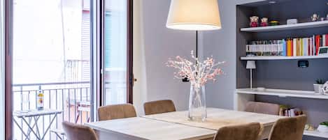 Uma área de refeições com mesa, cadeiras, luminária e estante de livros.