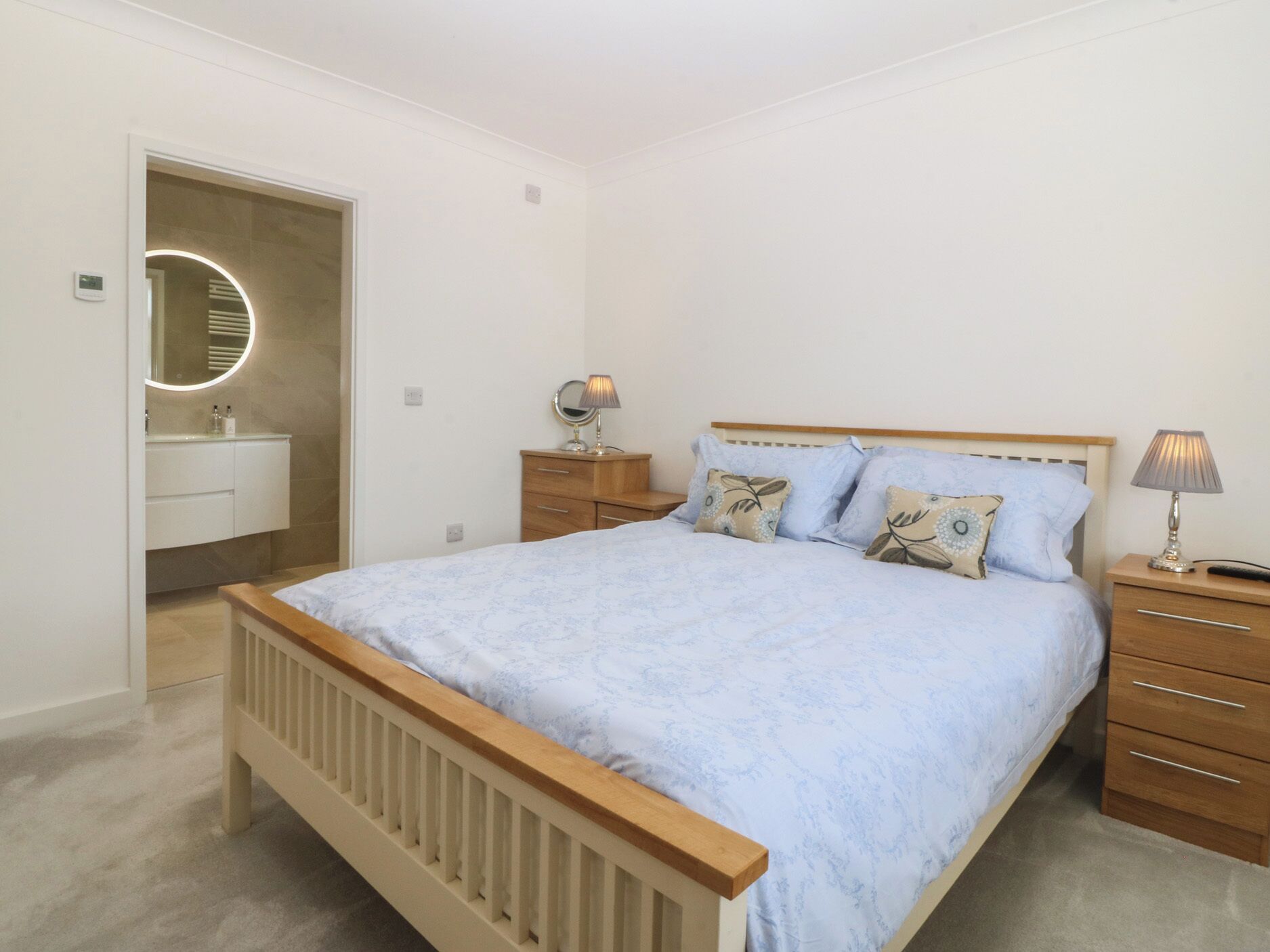 Quarto com cama, mesas de cabeceira, aparador, espelho e banheiro com pia e vaso sanitário.