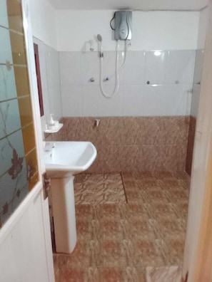 Uma casa de banho com lavatório, chuveiro e paredes em azulejo.