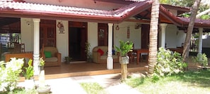 Varanda coberta com duas cadeiras, uma mesa e vasos de plantas.