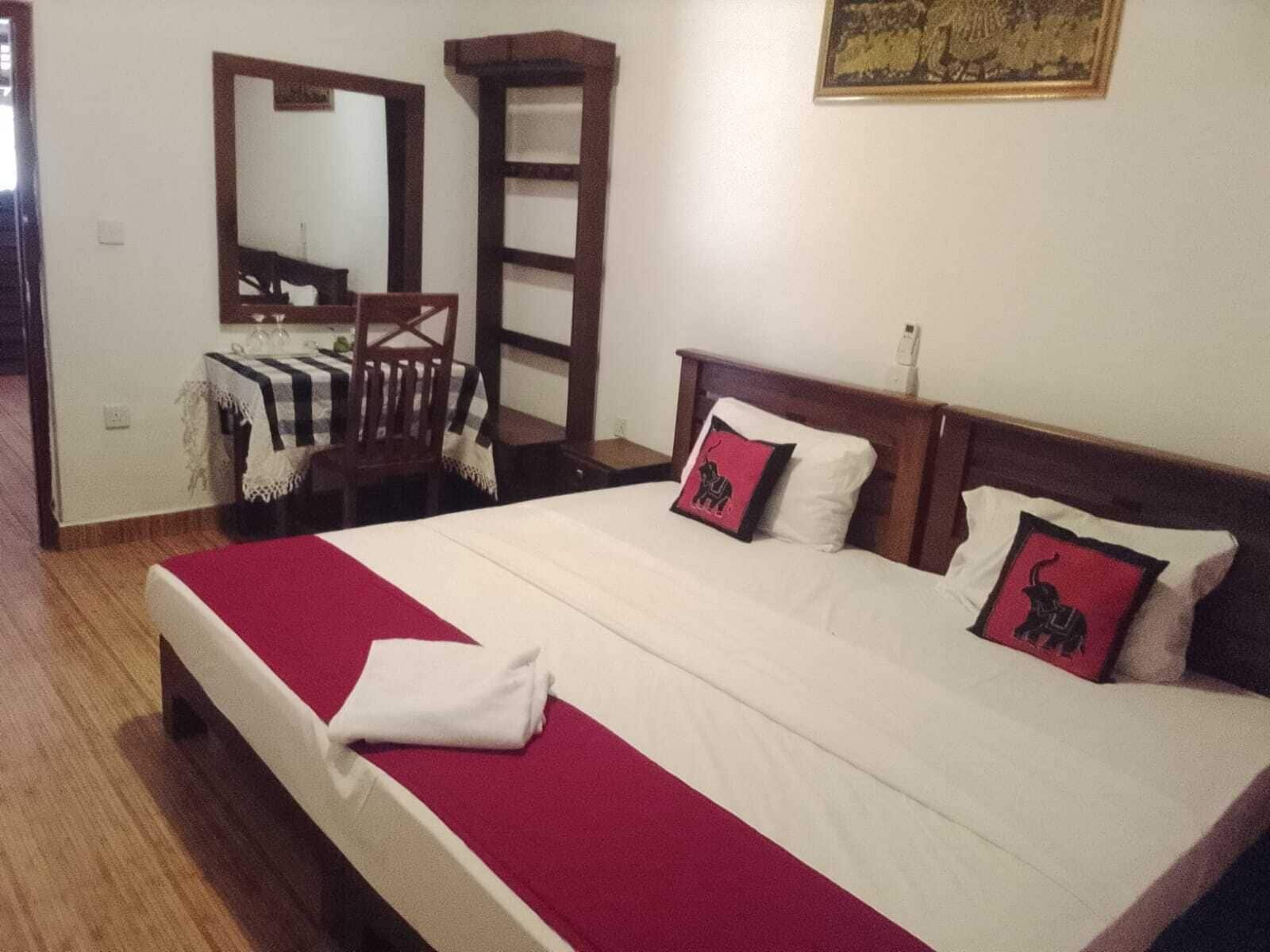 Quarto de hotel com cama, escrivaninha, cadeira e espelho.