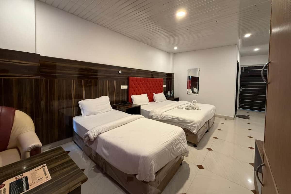 Quarto de hotel com duas camas, cabeceira de madeira, parede com destaque em vermelho, uma mesinha e uma cadeira.