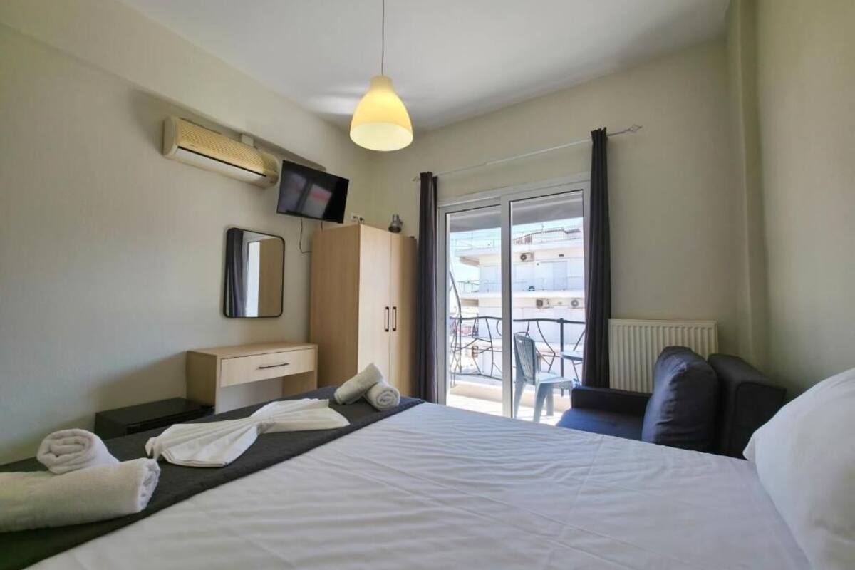 Quarto de hotel com cama, televisão, guarda-roupa, espelho e varanda com mesa e cadeiras.