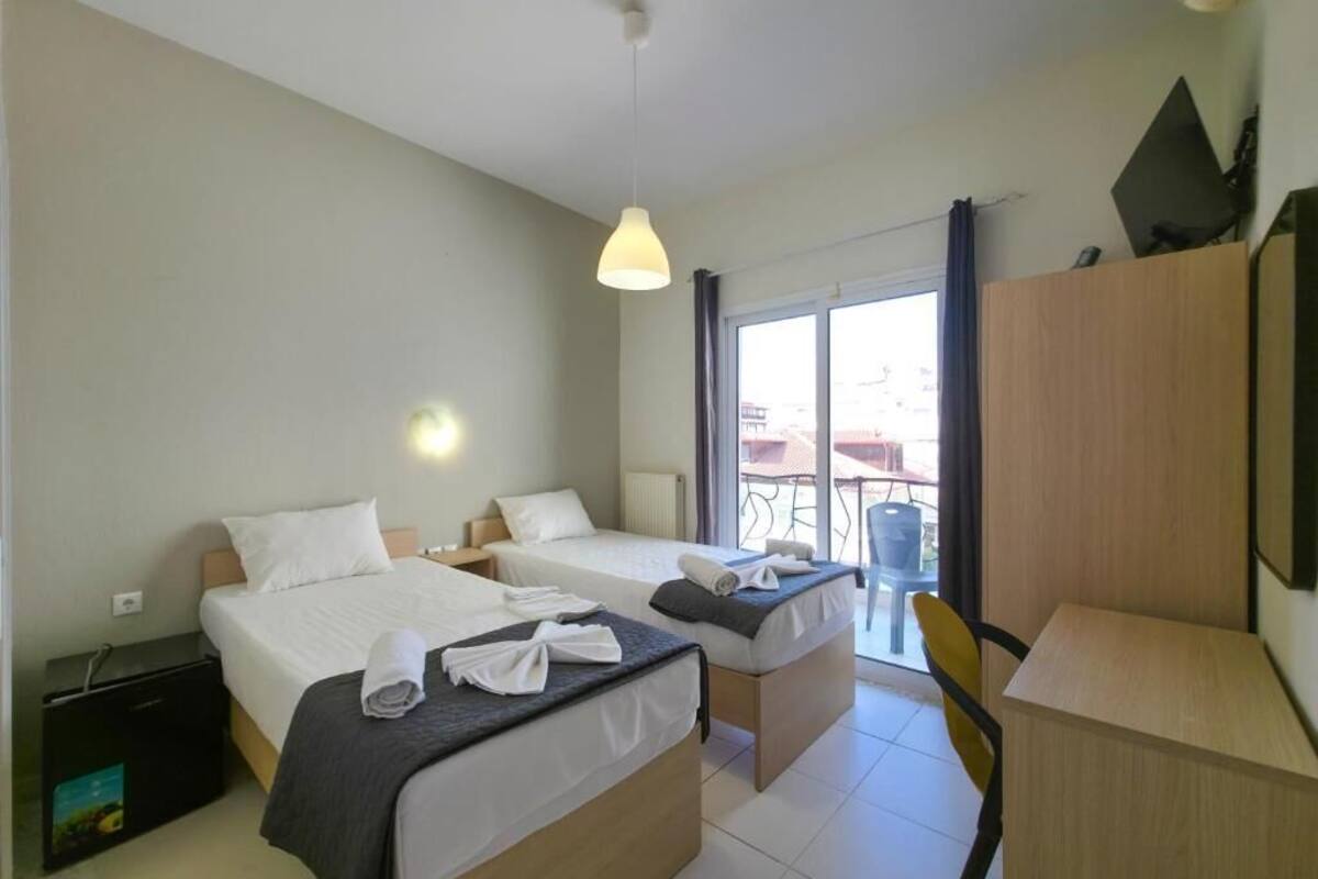 Quarto de hotel com duas camas, uma escrivaninha, uma cadeira, televisão e varanda com vista.