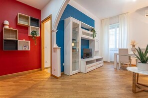 Uma sala de estar moderna com uma parede vermelha, um móvel branco para entretenimento e um espaço de jantar com mesa e cadeiras.