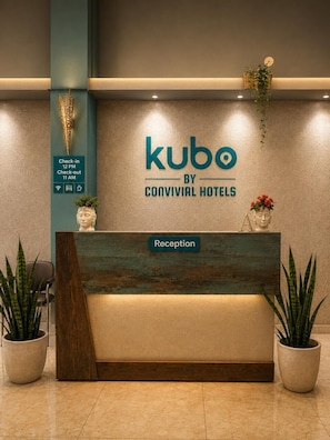 Balcão de recepção com placa de 'kubo by Convival Hotels', horários de check-in/check-out e identificação da recepção.