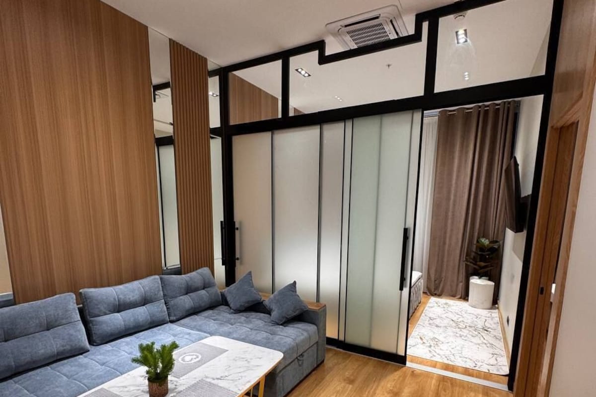 Uma sala de estar moderna com um sofá, uma mesa de centro e uma porta de vidro deslizante que dá para uma varanda.