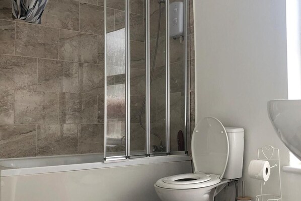 Casa de banho com cabine de duche, sanita e suporte para papel higiénico.